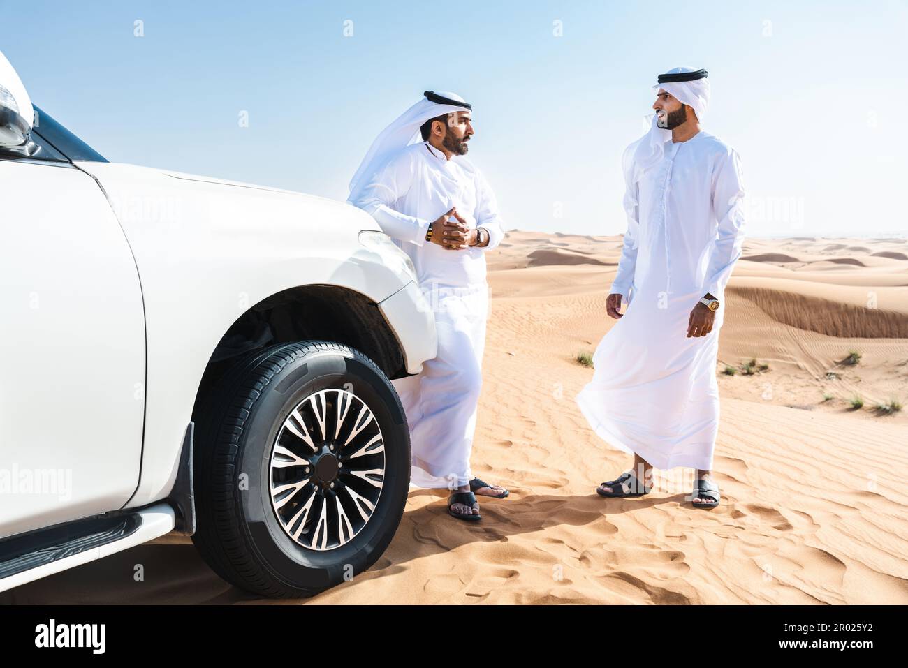 Two middle-eastern men wearing traditional emirati arab kandura driving ...
