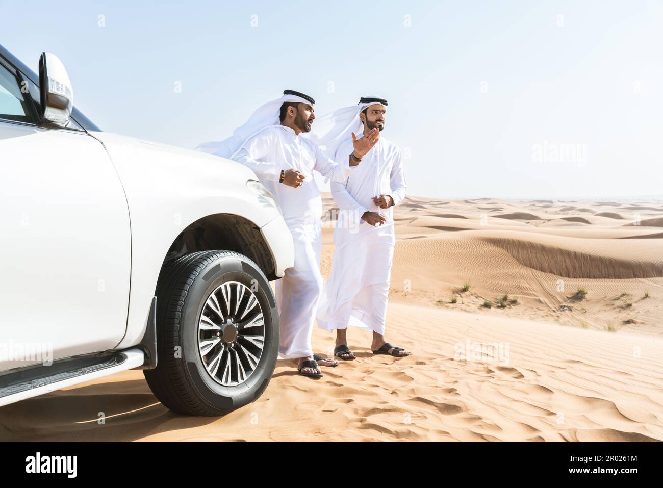 Two middle-eastern men wearing traditional emirati arab kandura driving ...