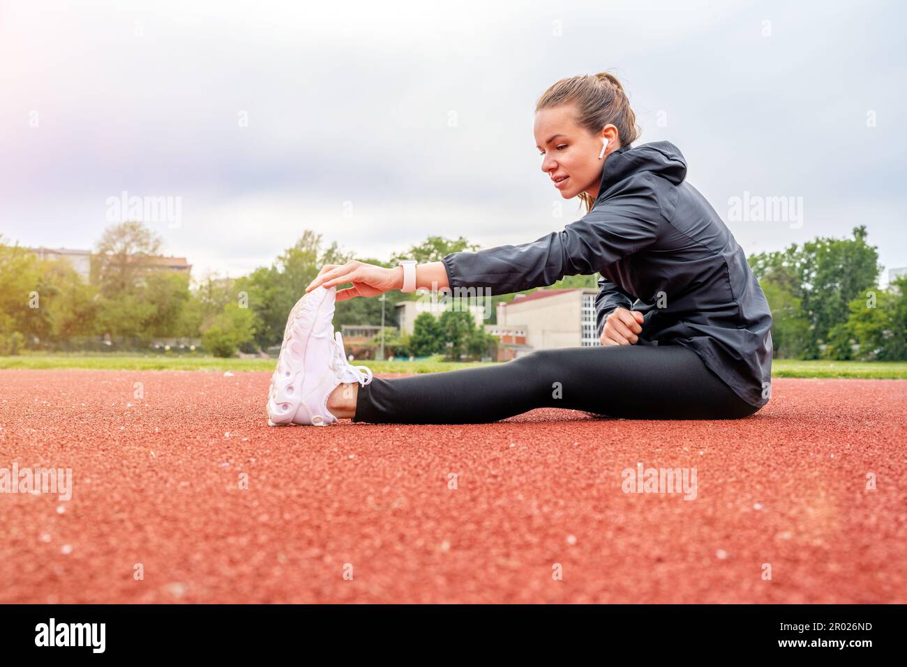 Young female athlete runner sitting on running track and stretching her ...