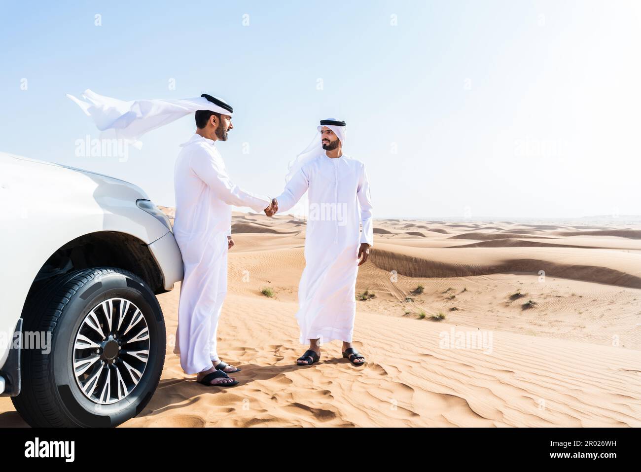 Two middle-eastern men wearing traditional emirati arab kandura driving ...