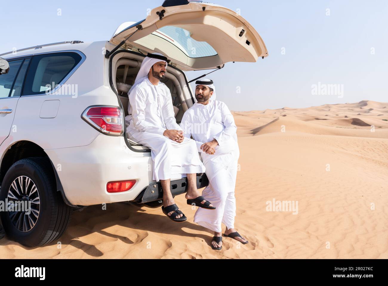 Two middle-eastern men wearing traditional emirati arab kandura driving ...