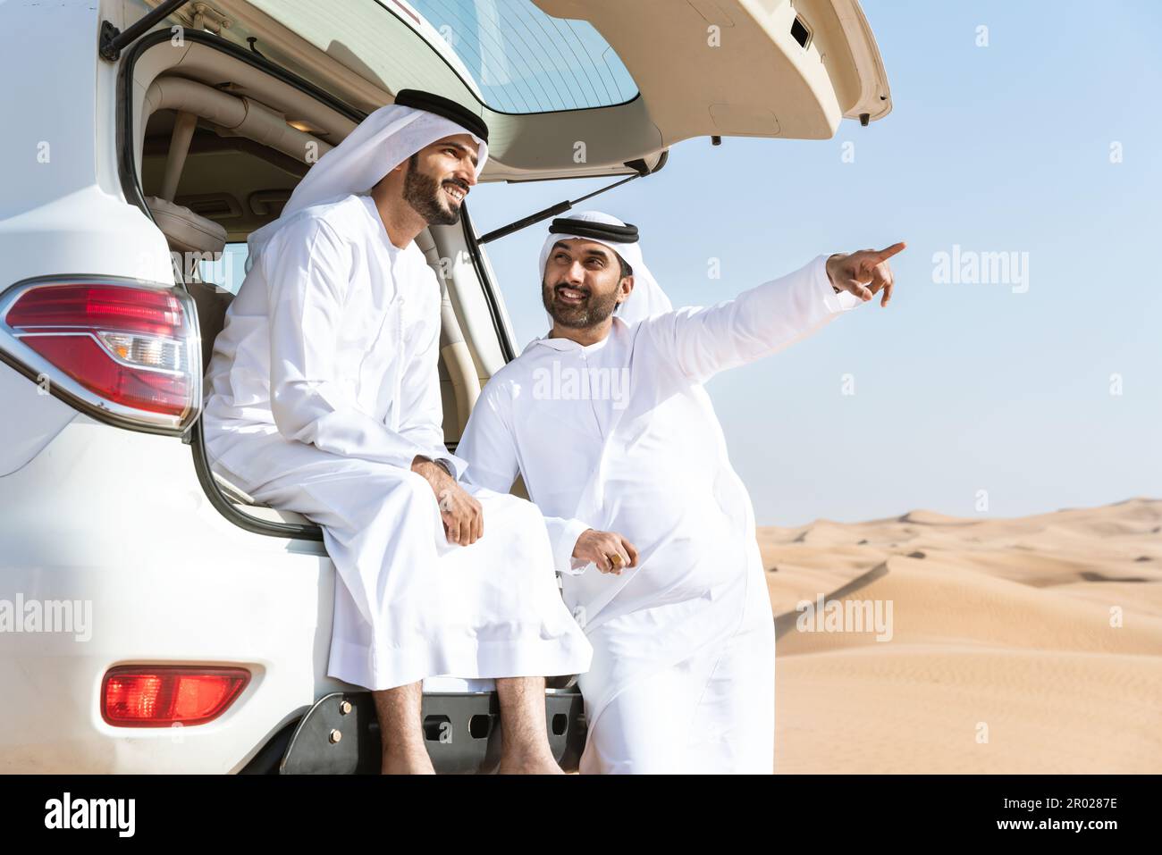 Two middle-eastern men wearing traditional emirati arab kandura driving ...
