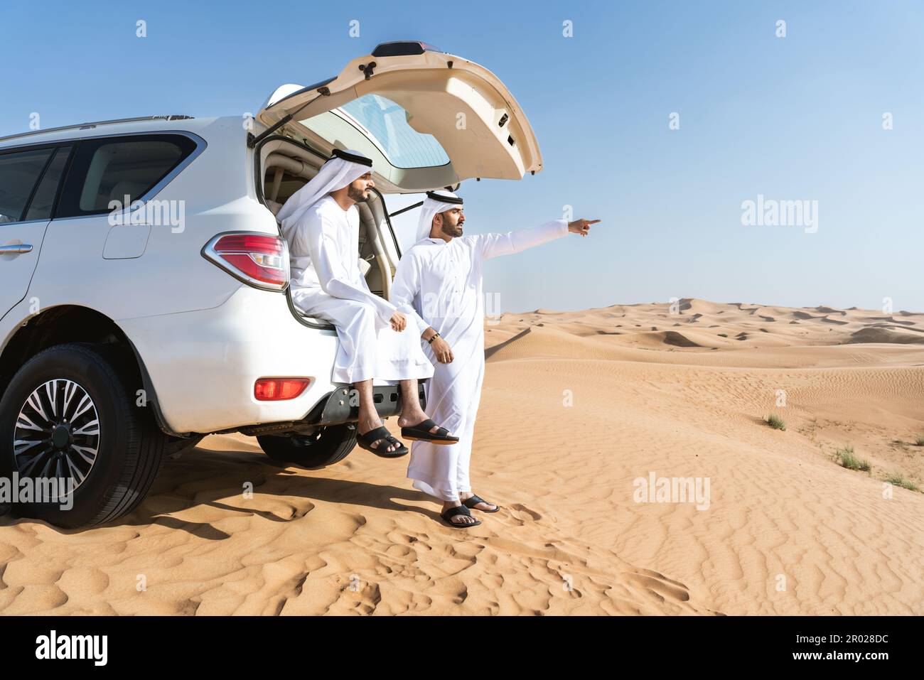 Two middle-eastern men wearing traditional emirati arab kandura driving ...