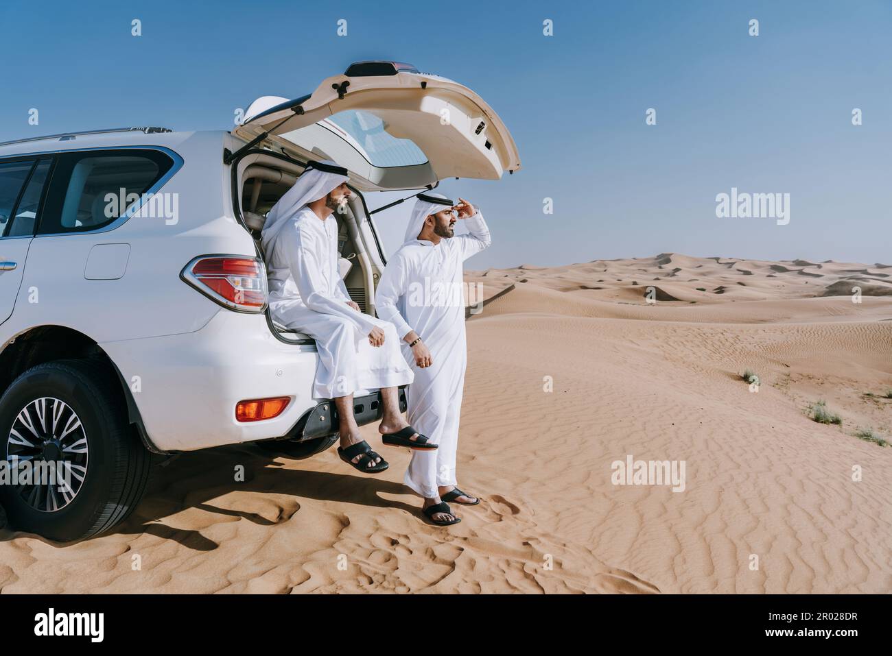 Two middle-eastern men wearing traditional emirati arab kandura driving ...