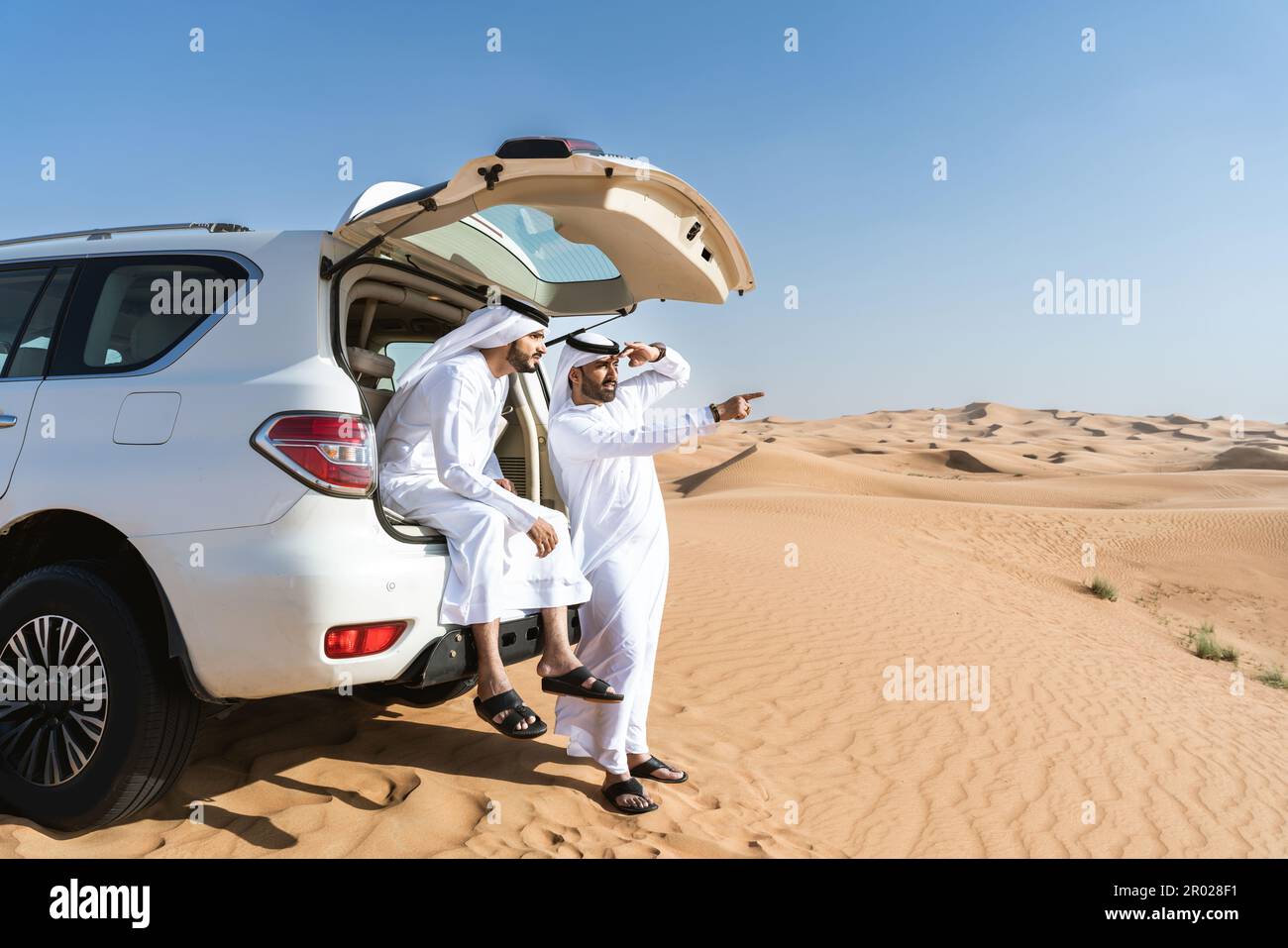 Two middle-eastern men wearing traditional emirati arab kandura driving ...