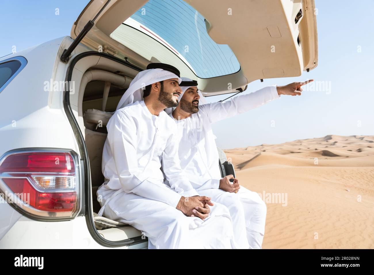Two middle-eastern men wearing traditional emirati arab kandura driving ...