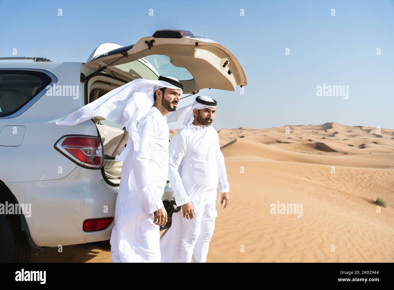 Two middle-eastern men wearing traditional emirati arab kandura driving ...