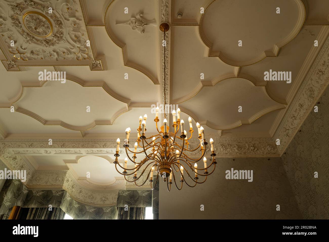 Large, lit chandelier seen hanging from an ornate plaster ceiling in a ...
