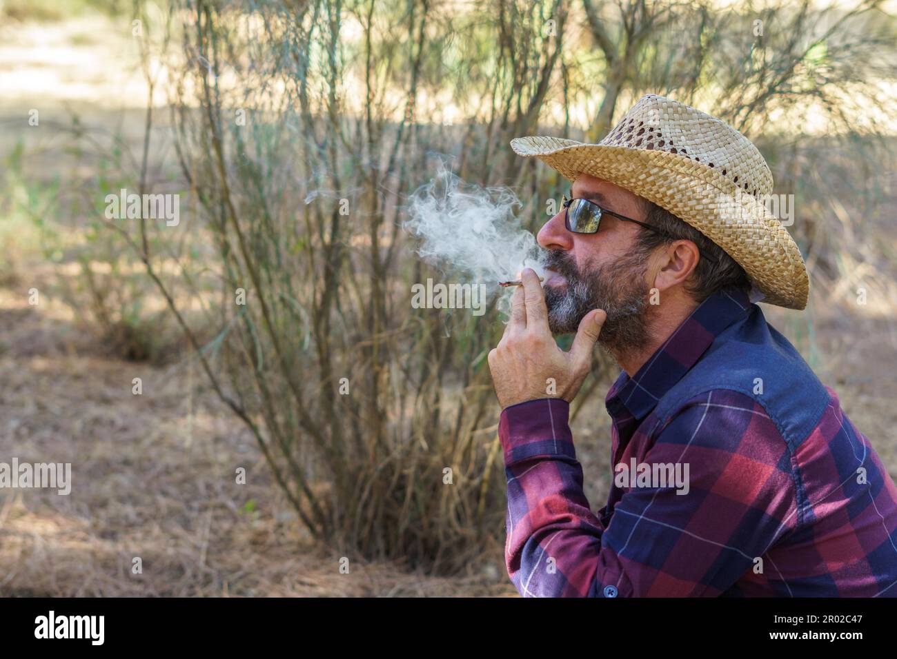 Man with beard and hat smoking a cigarette in the forest, fire hazard ...