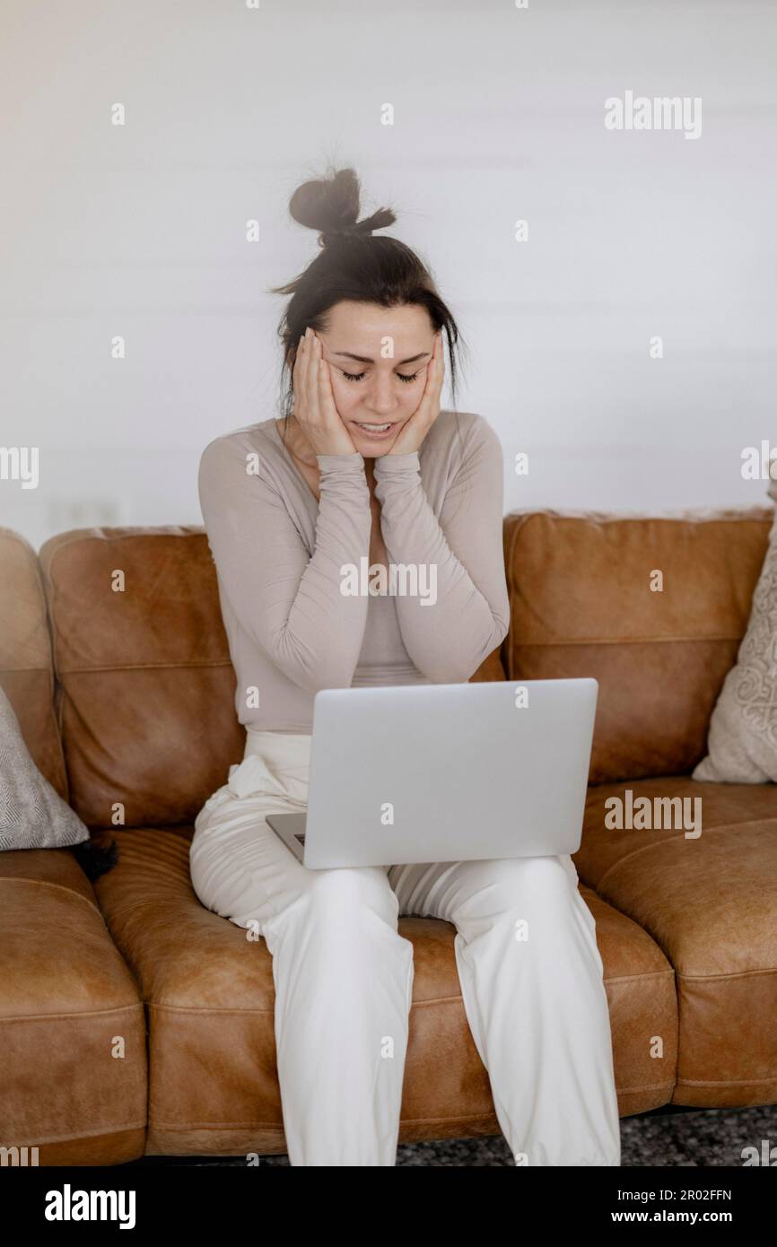 Woman sits on couch with laptop completely overwhelmed Stock Photo - Alamy