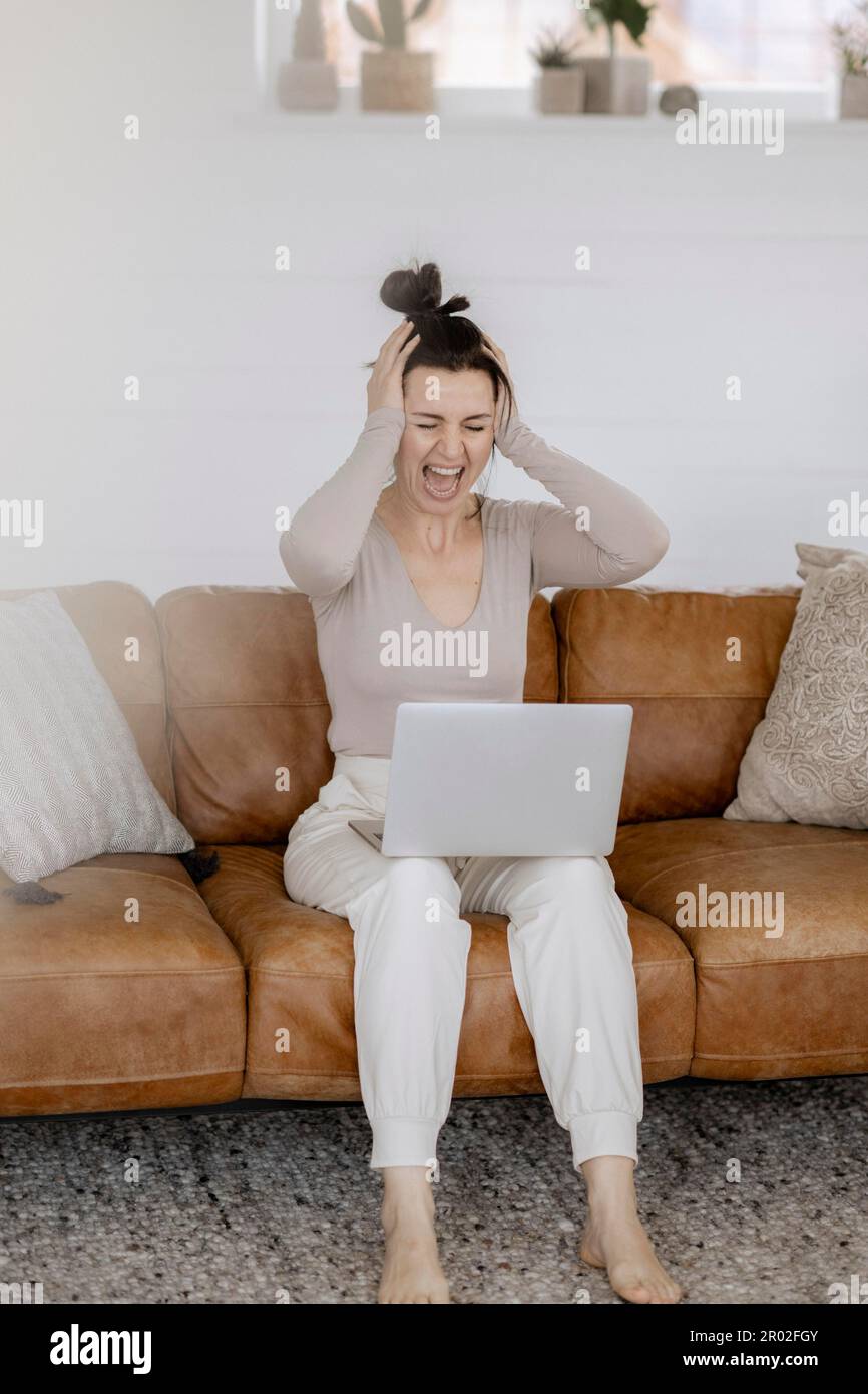 Woman sits on couch with laptop completely overwhelmed Stock Photo - Alamy