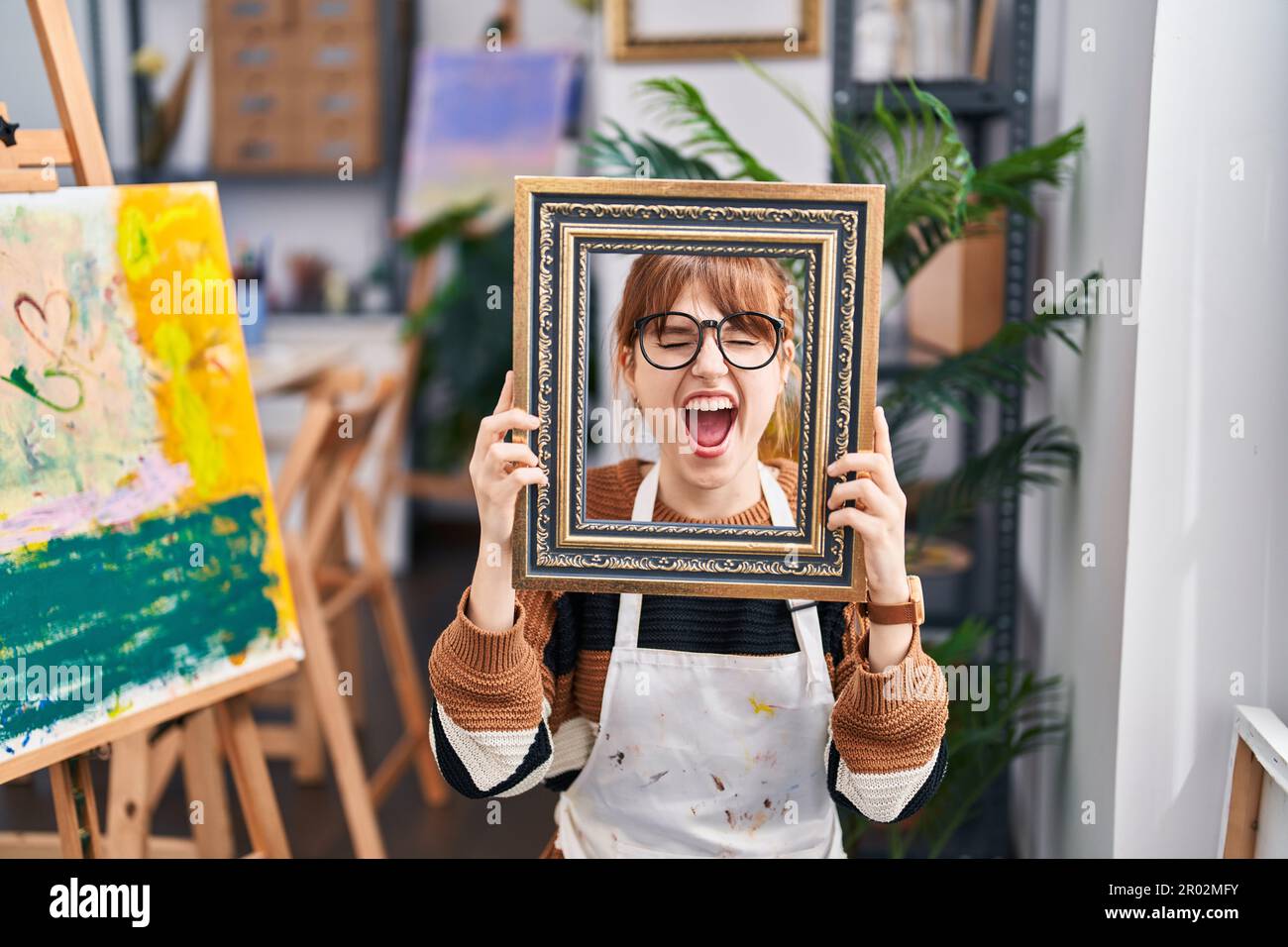 Young beautiful artist woman with face inside empty vintage frame angry ...