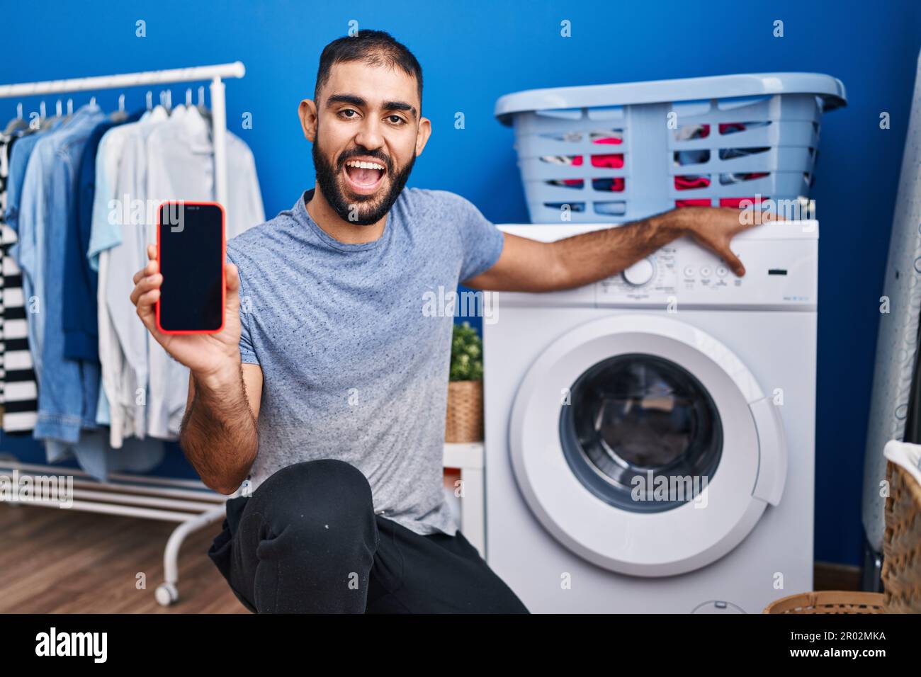 Middle east man with beard showing smartphone screen and washing ...