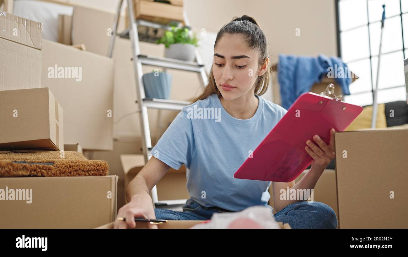 Young beautiful hispanic woman unpacking cardboard box writing on ...