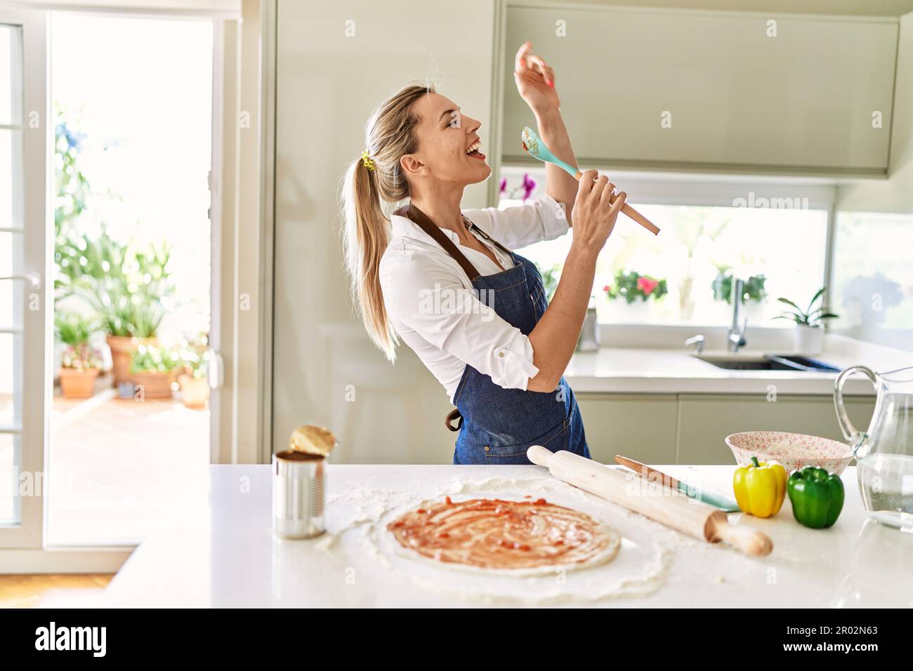 Young blonde woman singing song using spoon as a microphone cooking ...