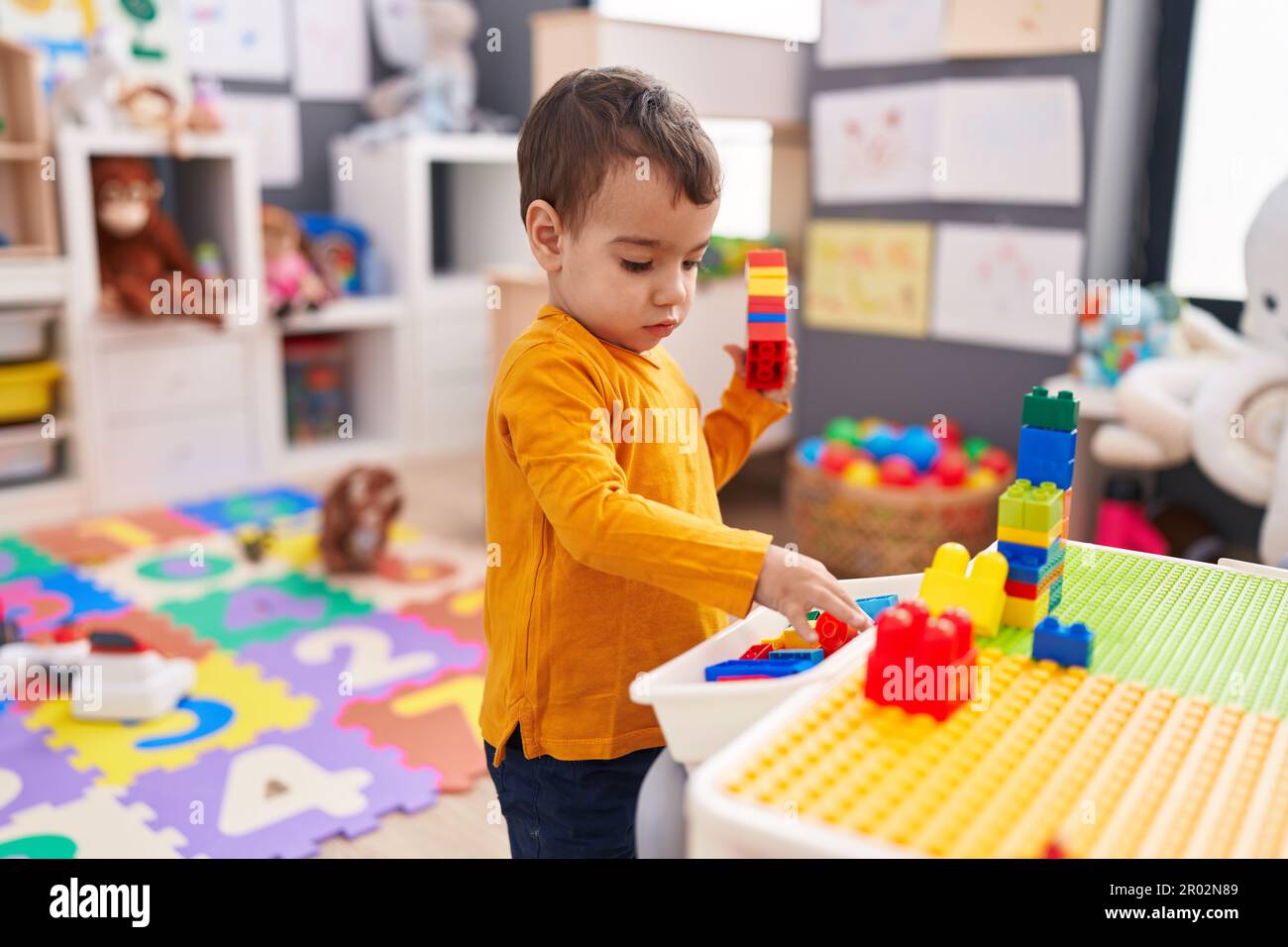 Adorable hispanic boy playing with construction blocks standing at ...