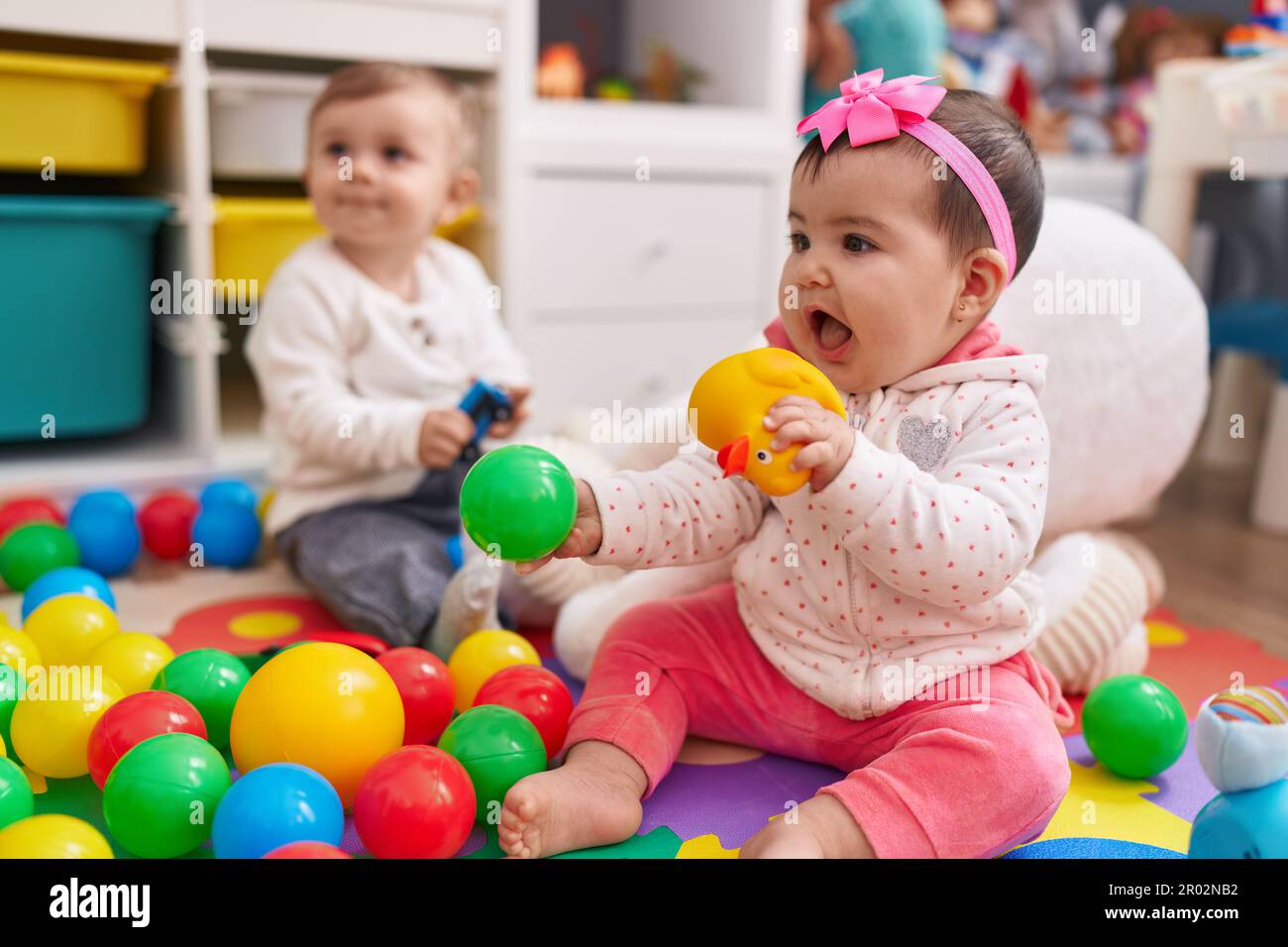 Adorable boy and girl playing with balls sitting on floor at ...