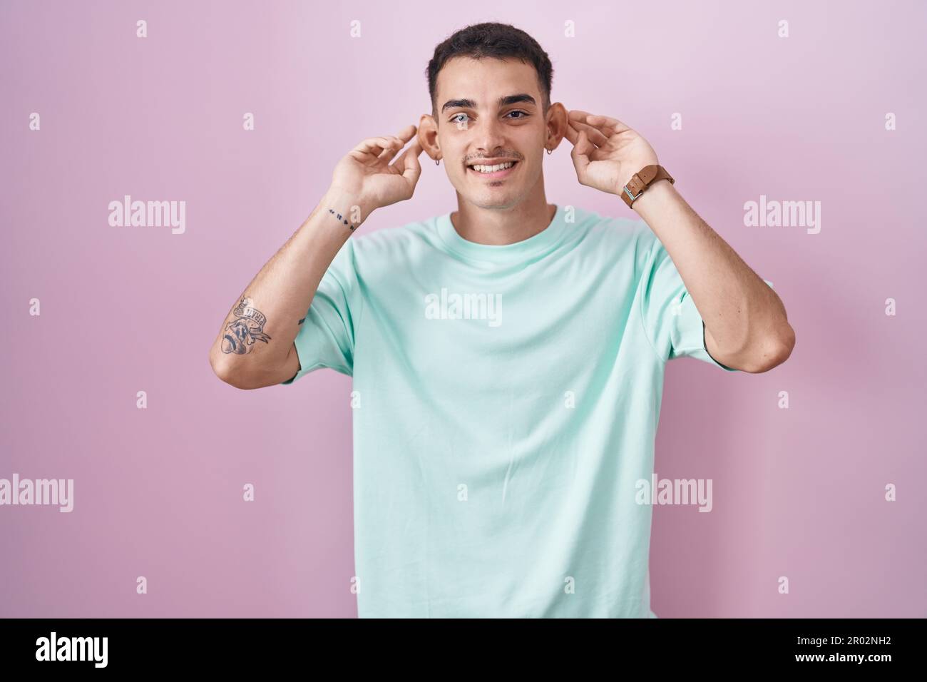 Handsome hispanic man standing over pink background smiling pulling ...