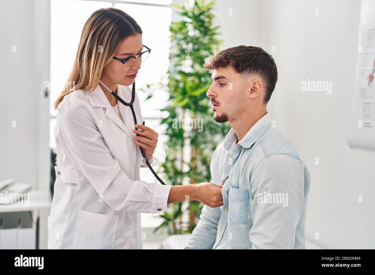 Young man and woman doctor and patient auscultating heart at clinic ...