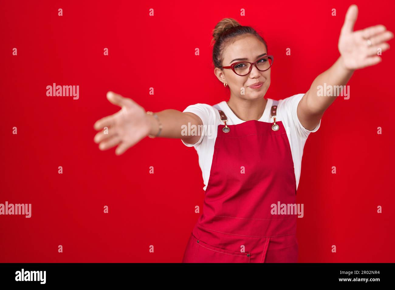 Young hispanic woman wearing waitress apron over red background looking ...