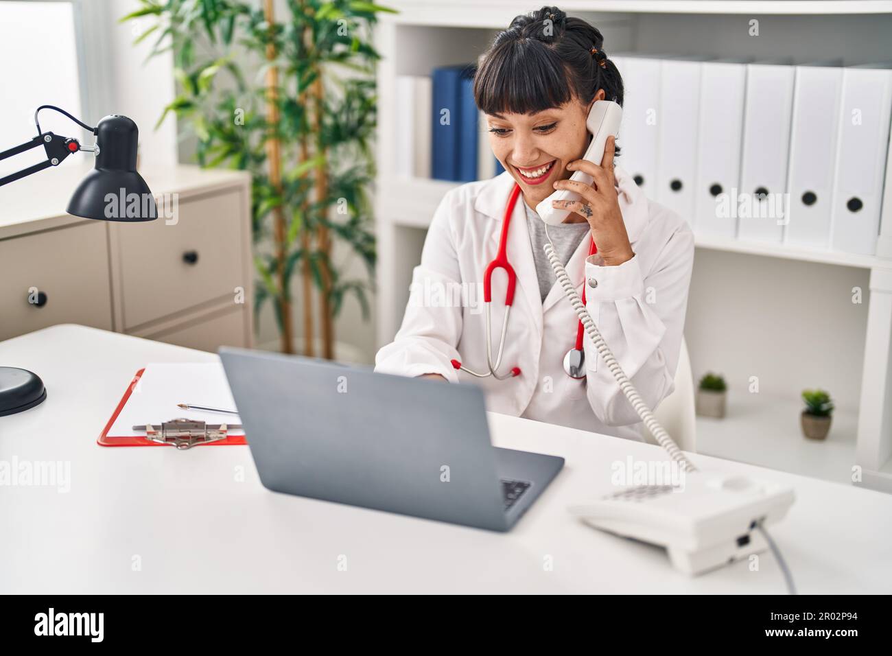 Young woman wearing doctor uniform talking on the telephone at clinic ...