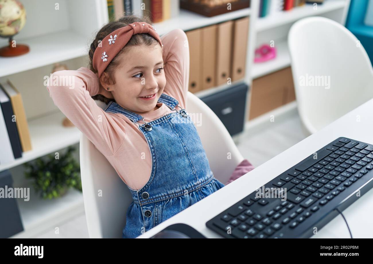 Adorable hispanic girl student using computer relaxed with hands on ...