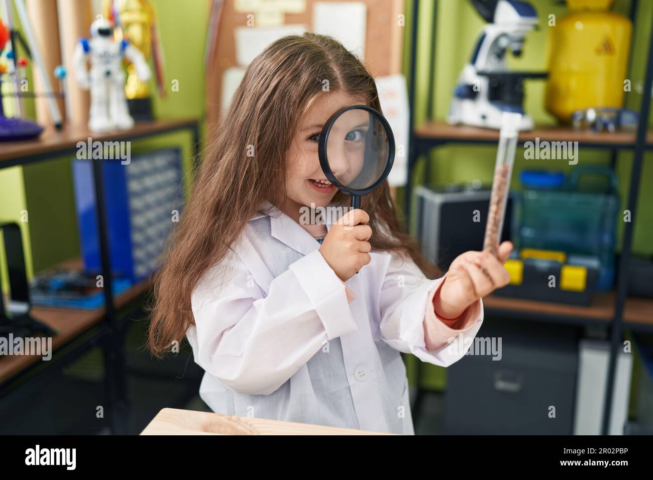 Adorable hispanic girl student looking sample with magnifying glass at ...