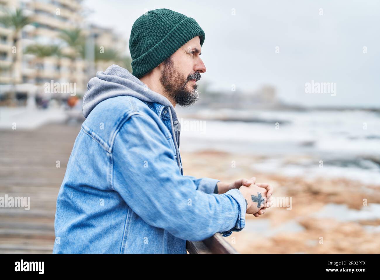 Young bald man leaning on balustrade with serious expression at seaside ...