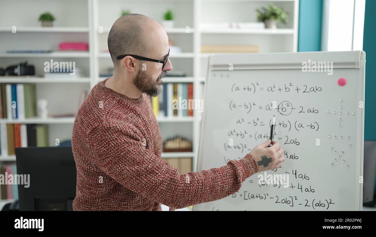 Young bald man teacher teaching maths on magnetic board at university ...