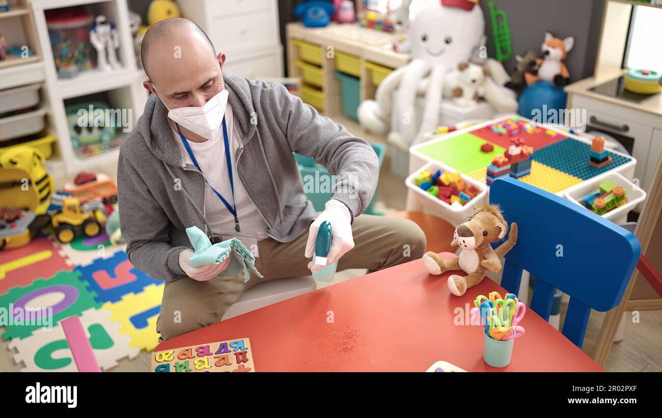 Young bald man preschool teacher wearing medical mask cleaning table at ...
