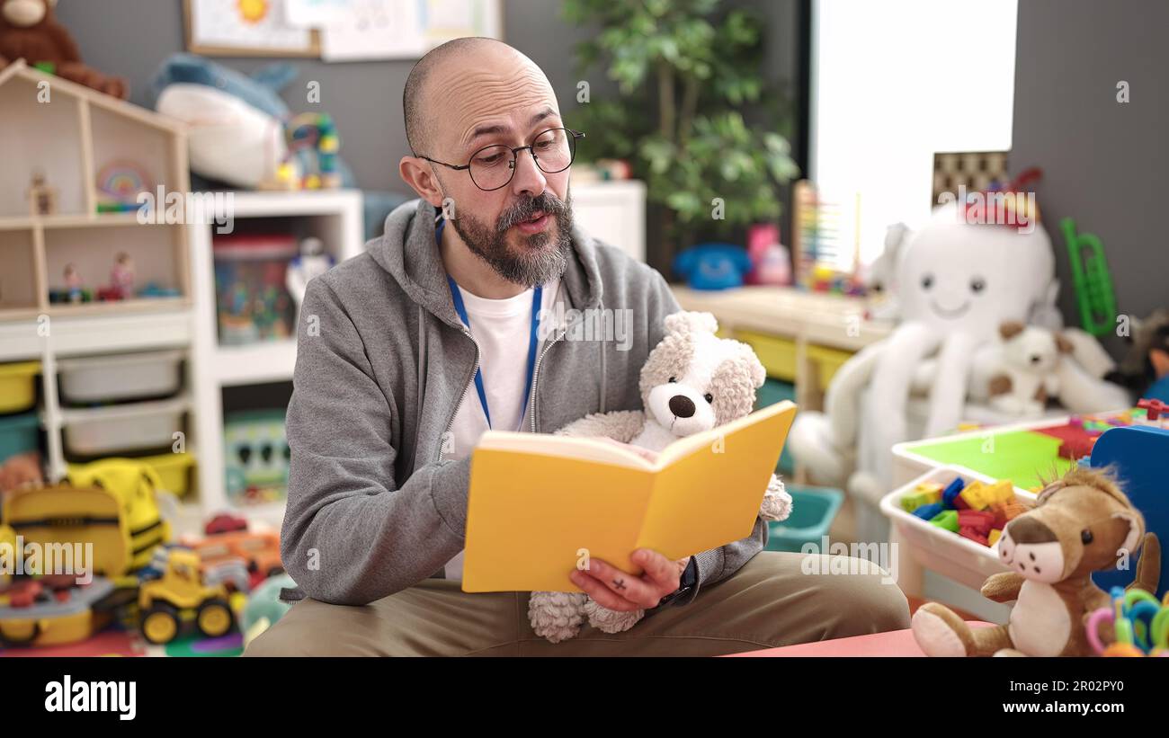 Young bald man preschool teacher reading story book at kindergarten ...