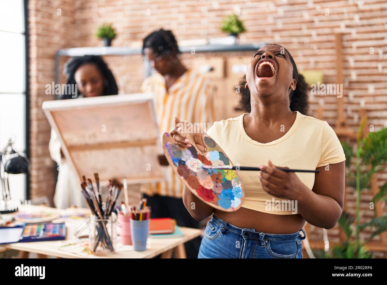 Young black painter woman at art studio holding palette angry and mad ...