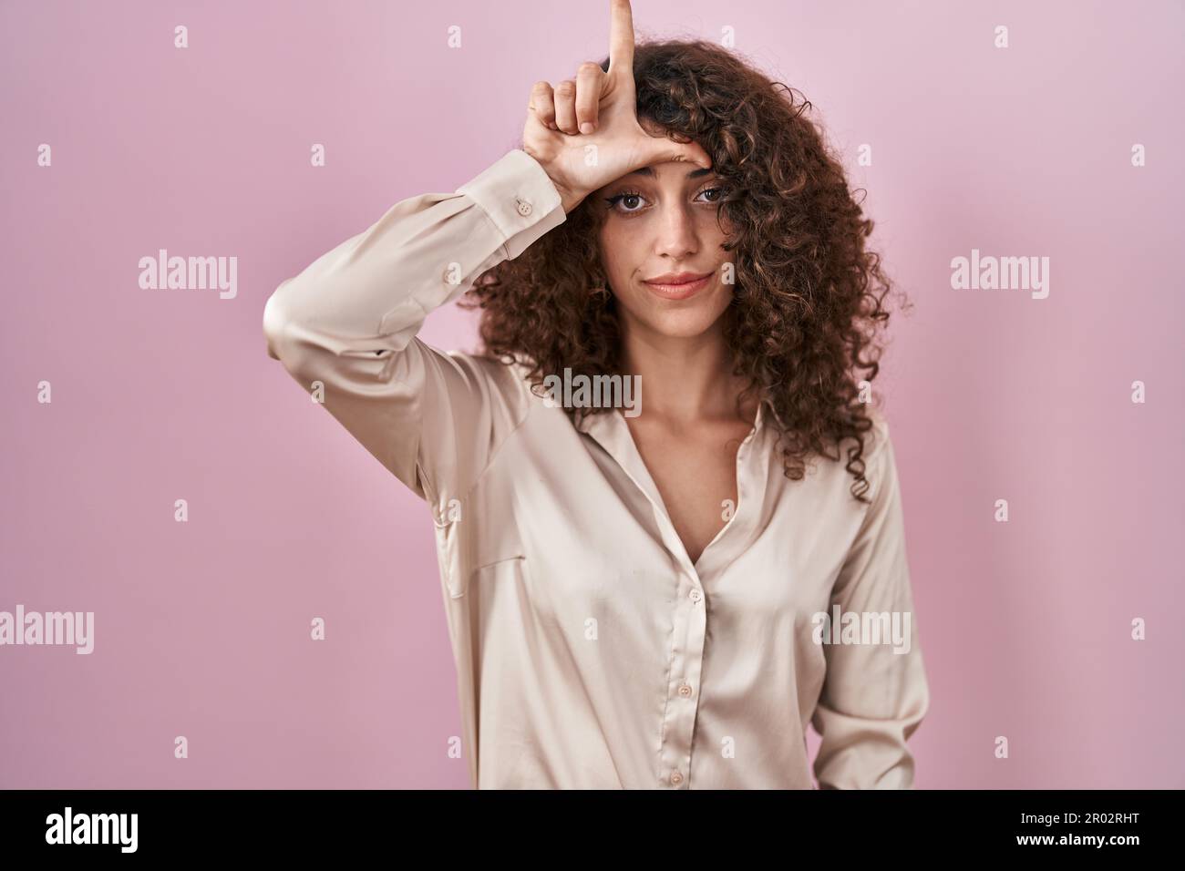 Hispanic woman with curly hair standing over pink background making fun ...
