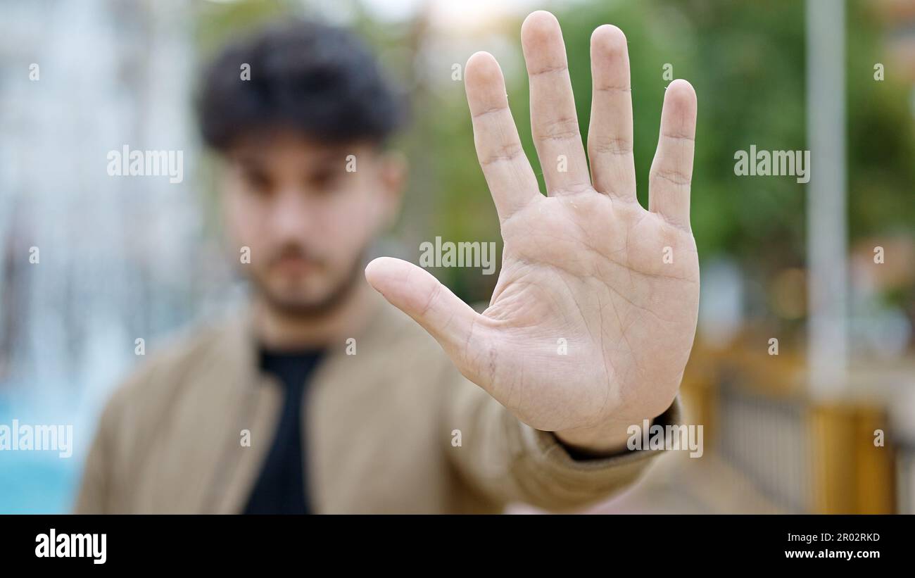 Young hispanic man doing stop gesture with hand at park Stock Photo - Alamy