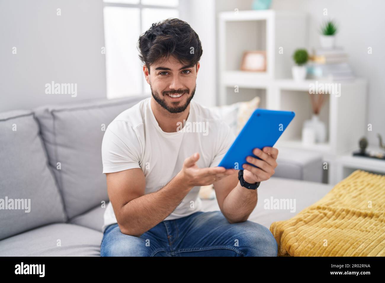 Hispanic Man With Beard Using Touchpad Sitting On The Sofa Pointing