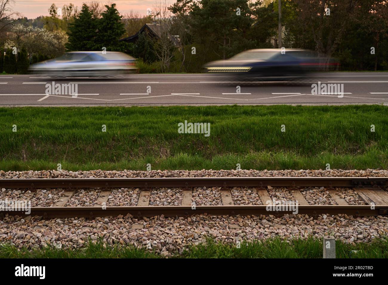 Blurred outlines of cars driving along a paved road next to a railway ...