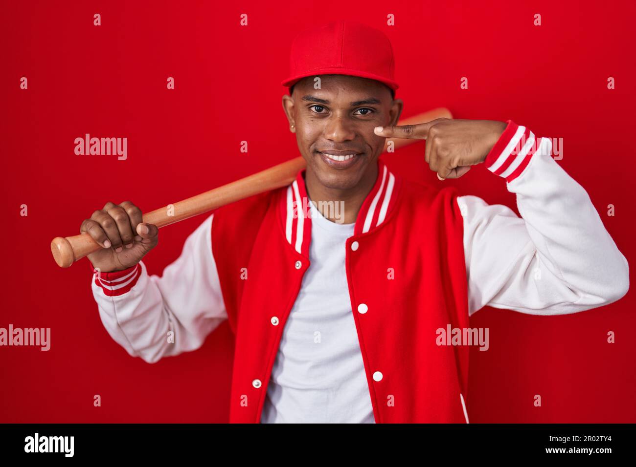 Young hispanic man playing baseball holding bat pointing with hand ...