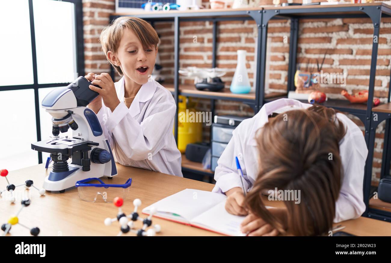 Adorable boys students using microscope writing notes at laboratory ...