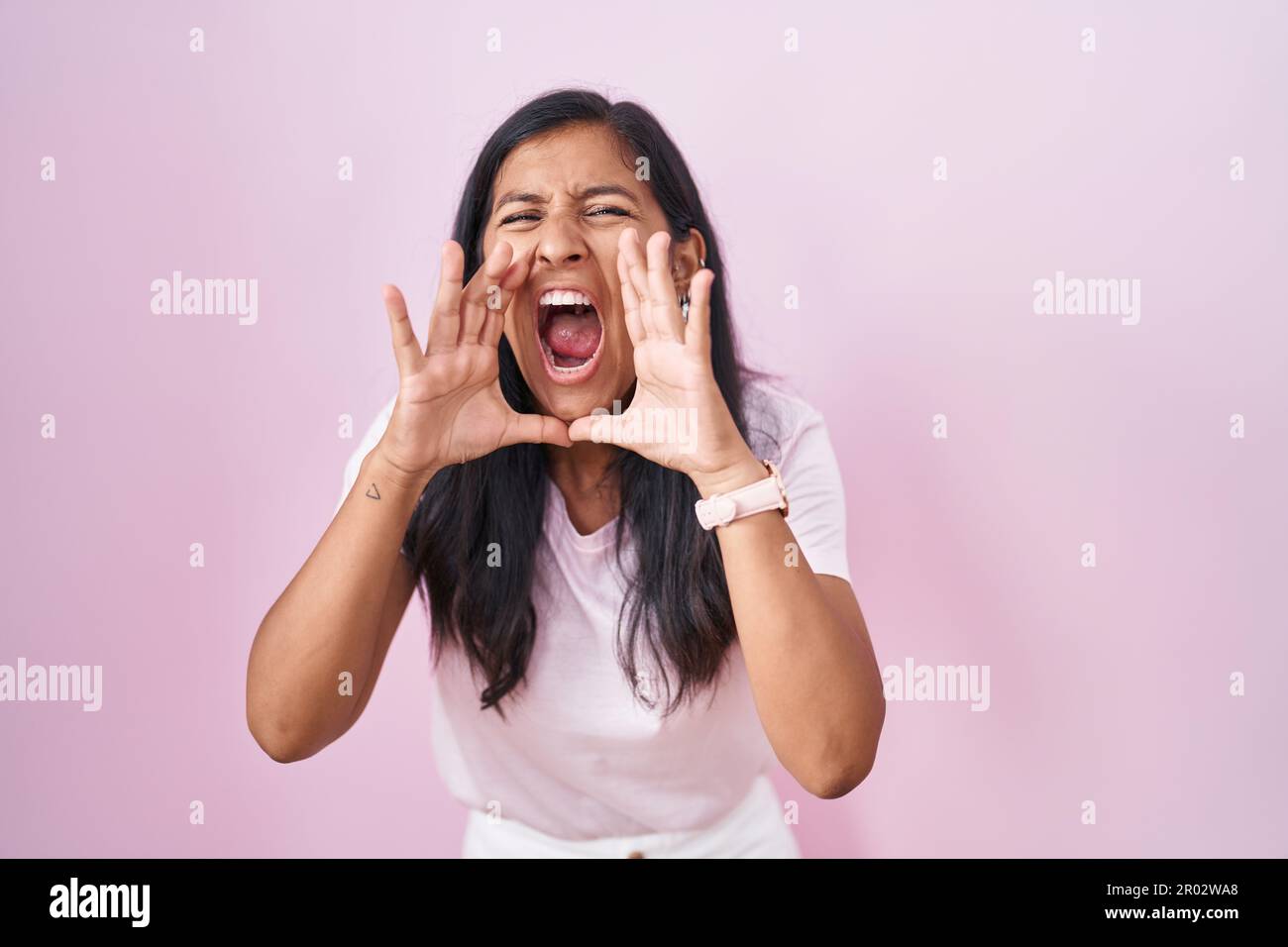 Young hispanic woman standing over pink background shouting angry out ...
