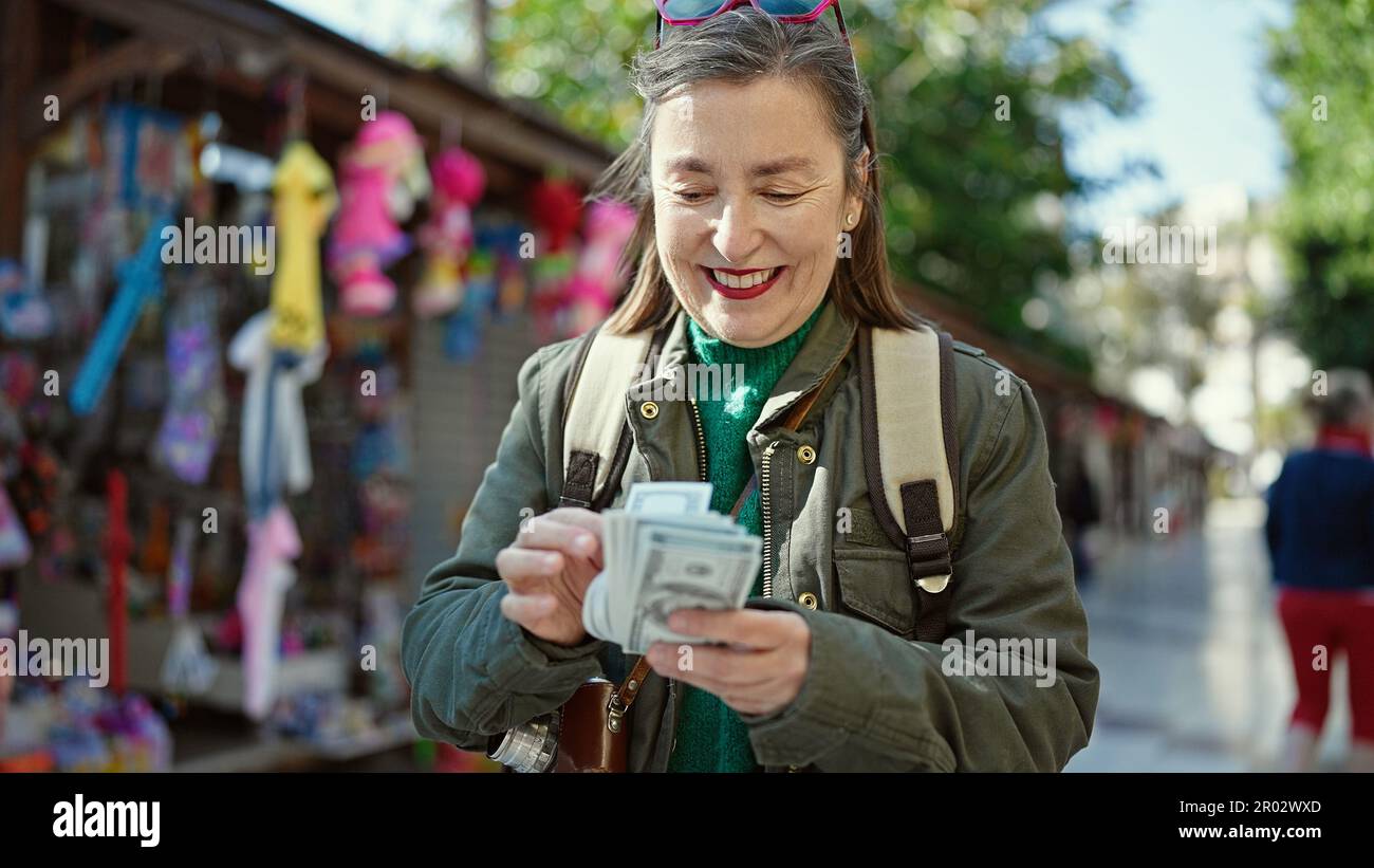 Mature hispanic woman with grey hair tourist wearing backpack counting ...