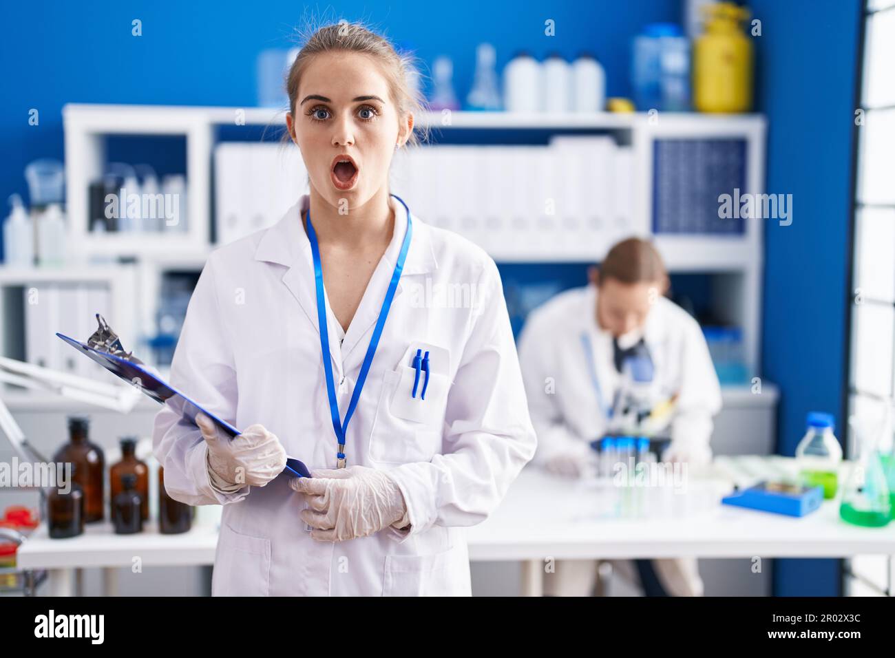 Blonde woman working at scientist laboratory scared and amazed with ...