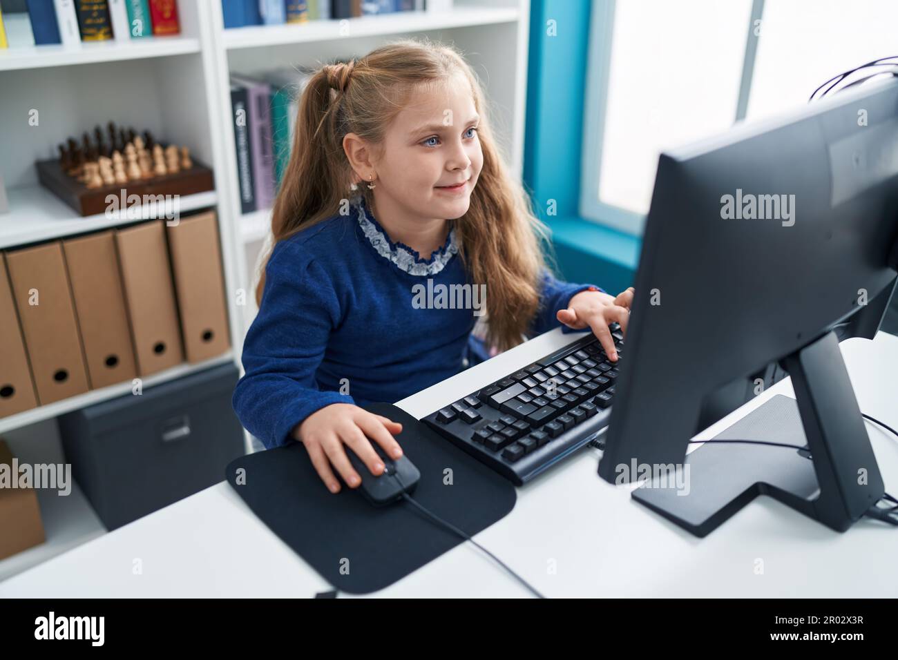 Adorable blonde girl student using computer sitting on table at ...