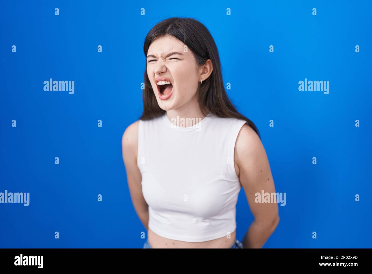 Young caucasian woman standing over blue background angry and mad ...