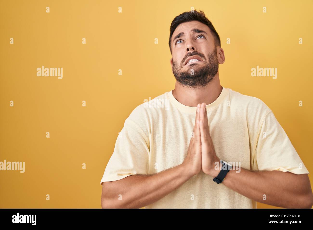 Handsome hispanic man standing over yellow background begging and ...