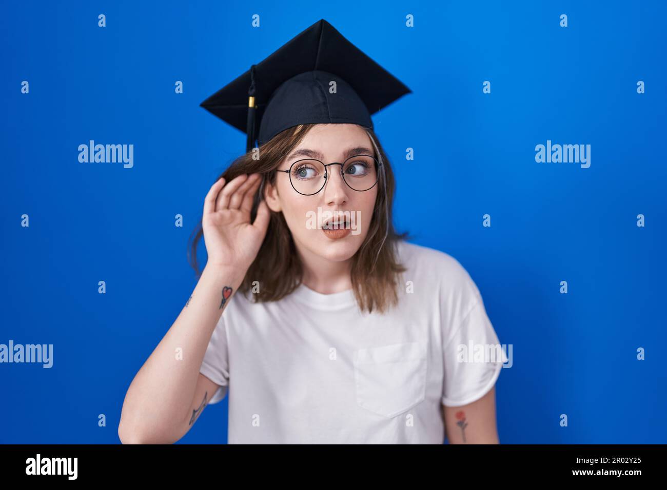 Blonde caucasian woman wearing graduation cap smiling with hand over ...