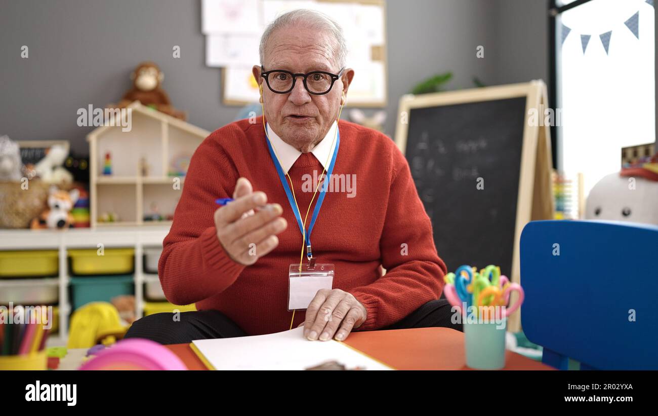 senior working as teacher writing on papers and talking at kindergarten ...