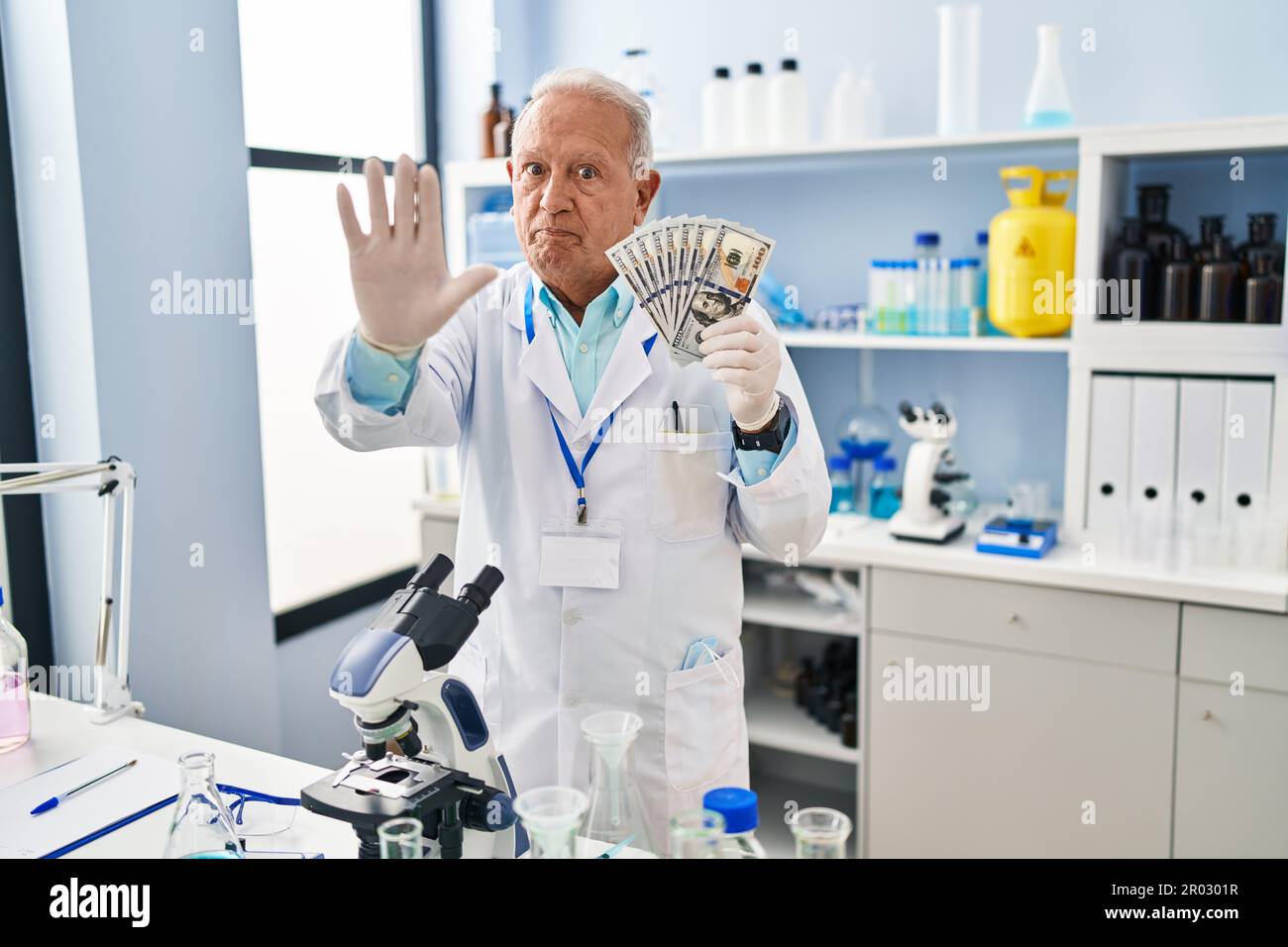 Senior scientist with grey hair working at laboratory holding dollars ...