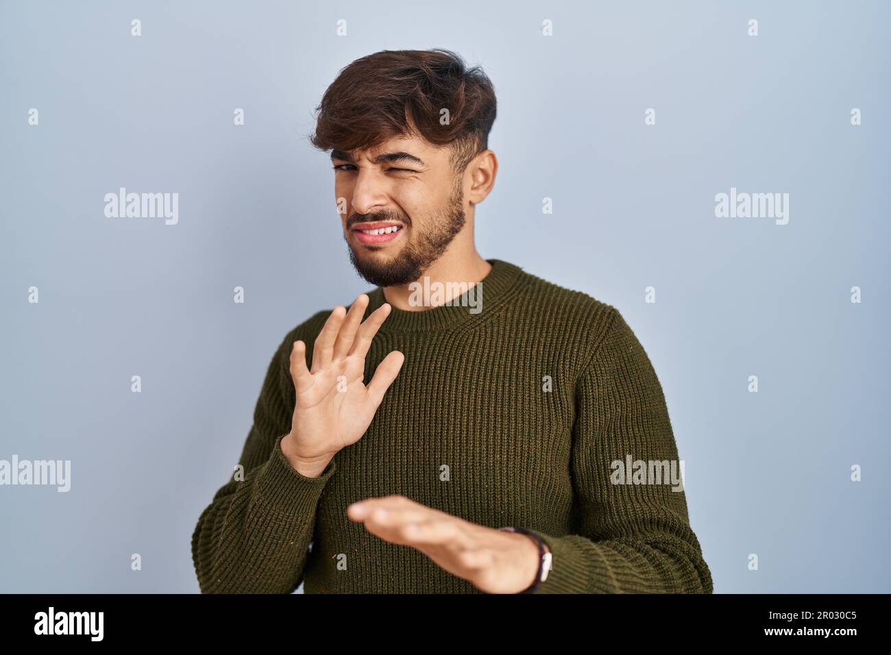 Arab man with beard standing over blue background disgusted expression ...