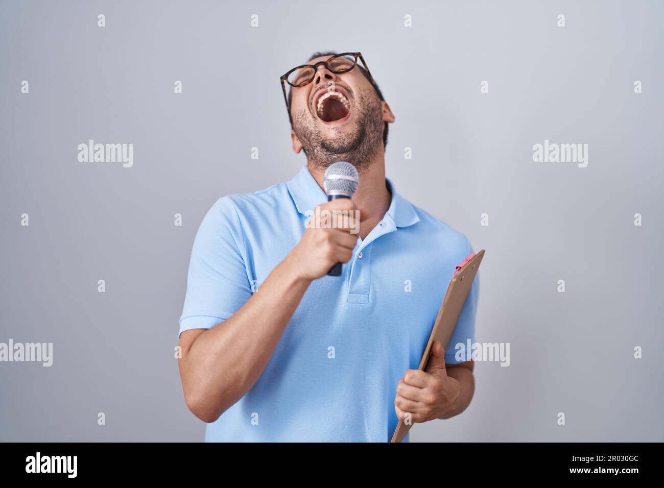 Hispanic man holding reporter microphone and clipboard angry and mad ...