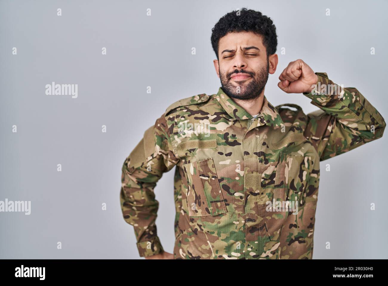 Arab man wearing camouflage army uniform stretching back, tired and ...